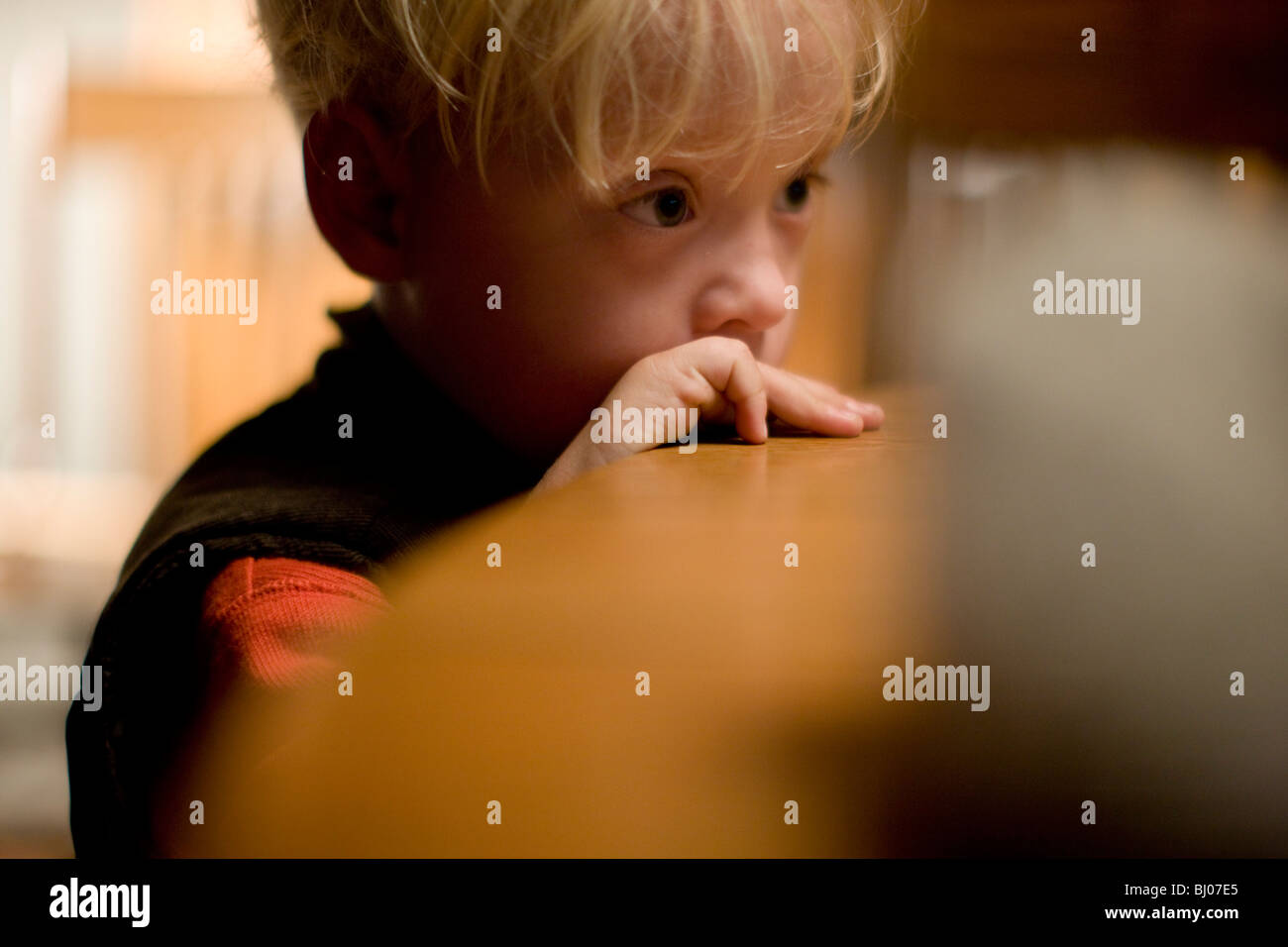 Young boy leaning on edge of table in thought Stock Photo - Alamy