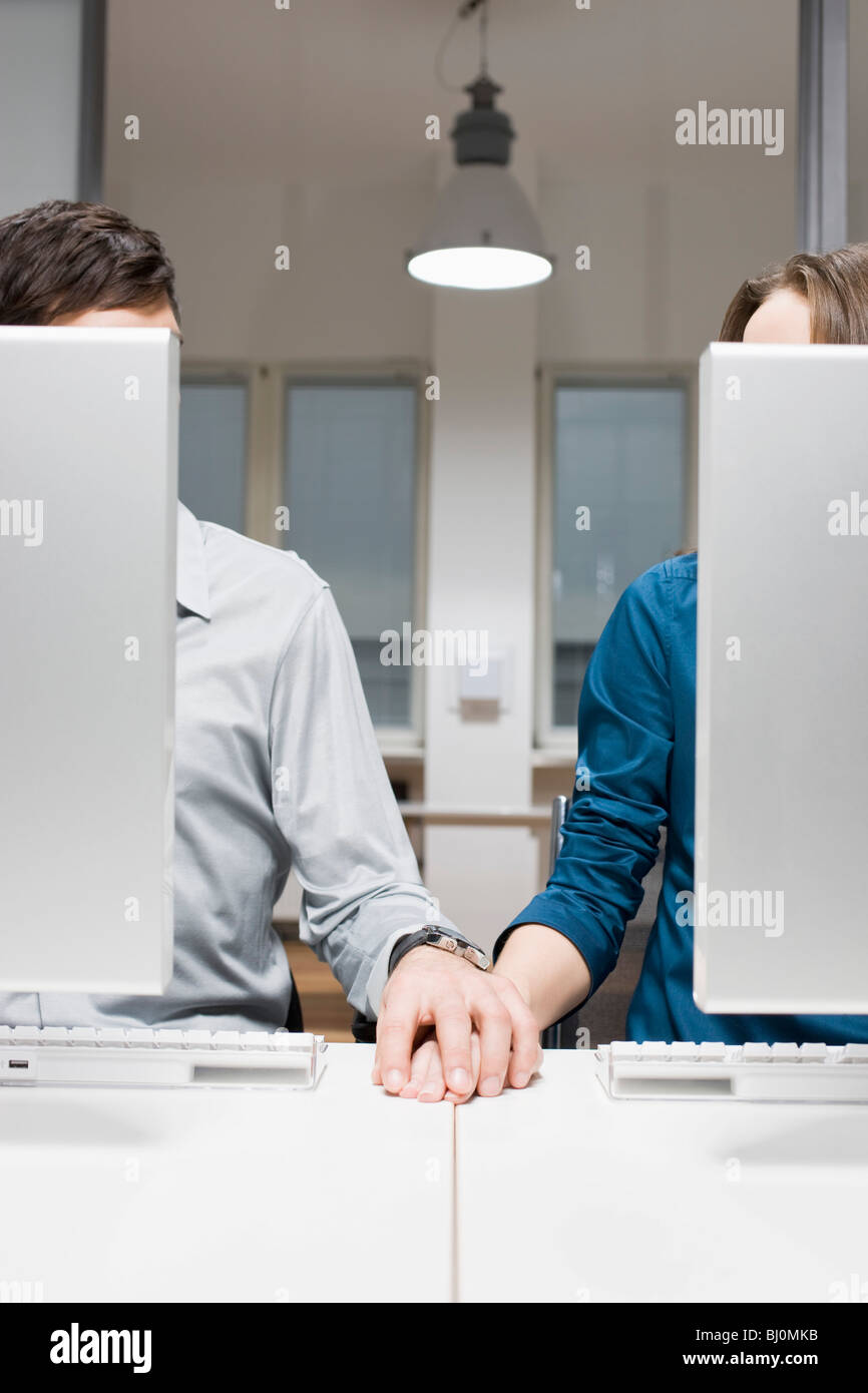 young couple sitting behind computers in office holding hands Stock ...