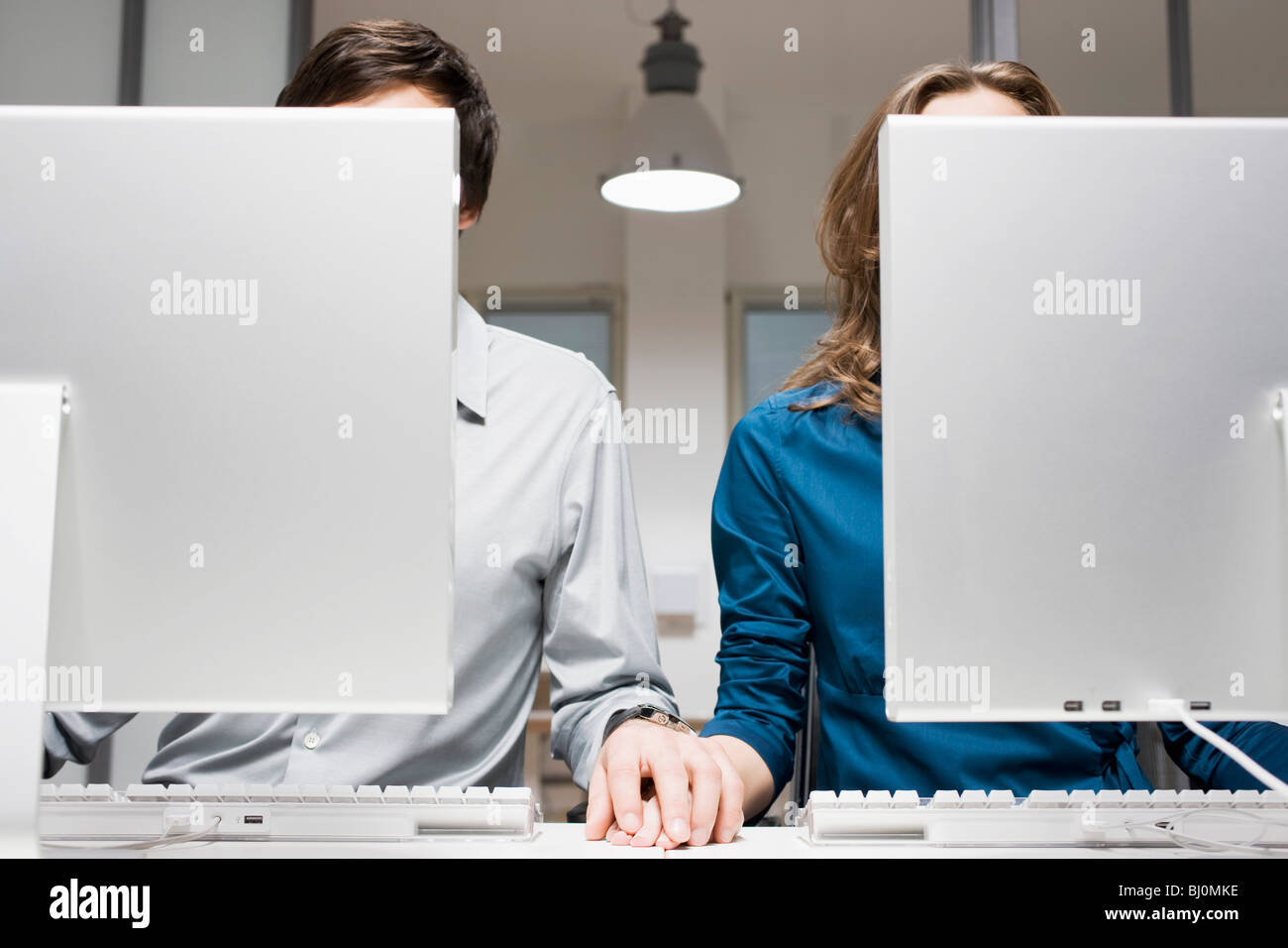 young couple sitting behind computers in office holding hands Stock ...