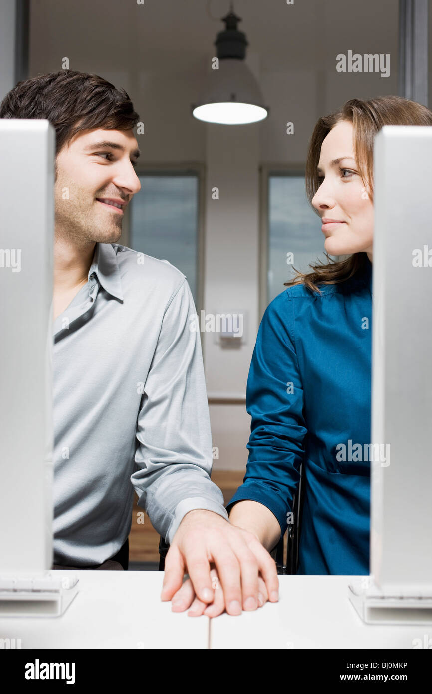 young couple sitting behind computers in office holding hands Stock ...