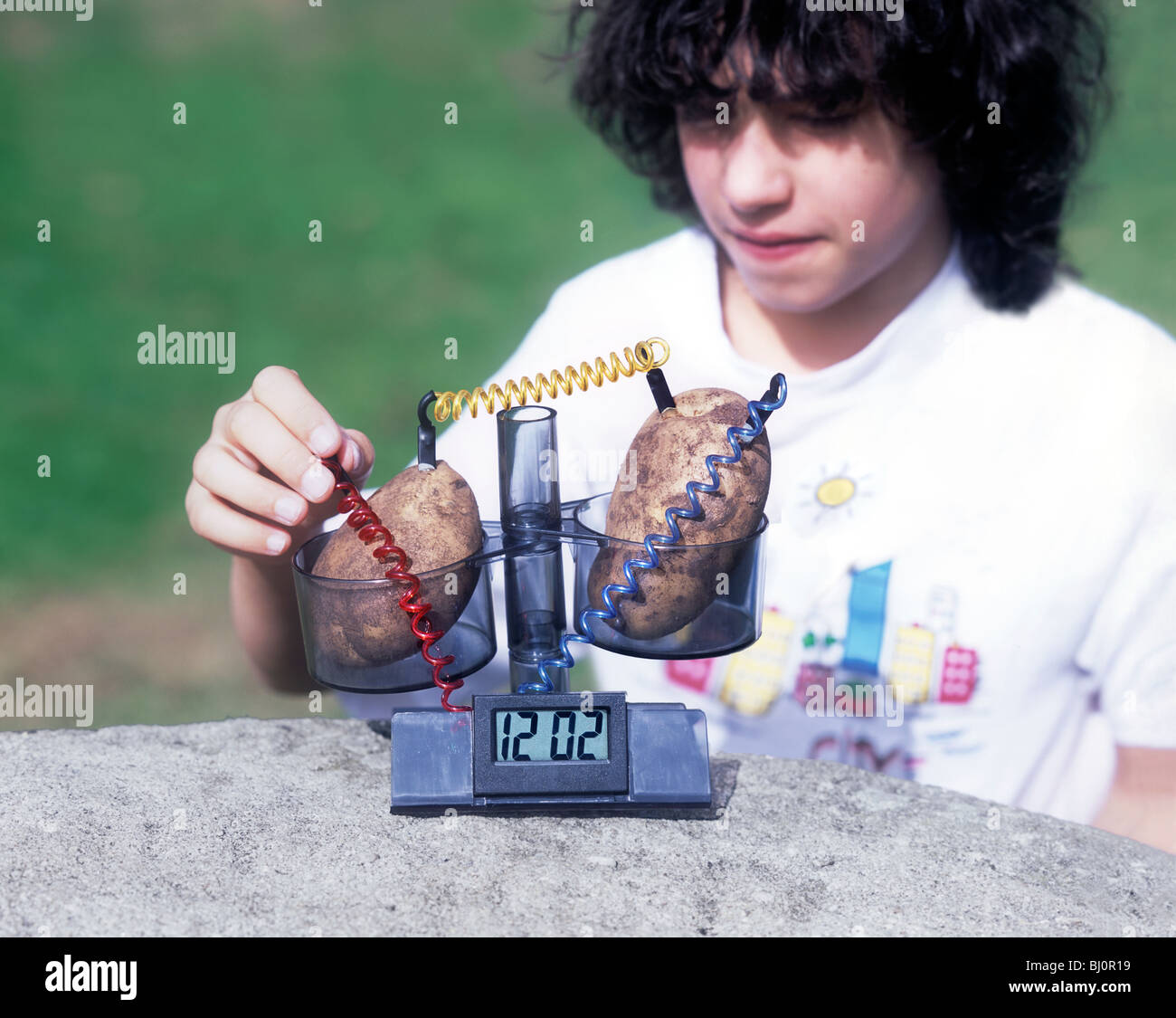 Schoolboy assembling a digital clock powered by an electric current ...