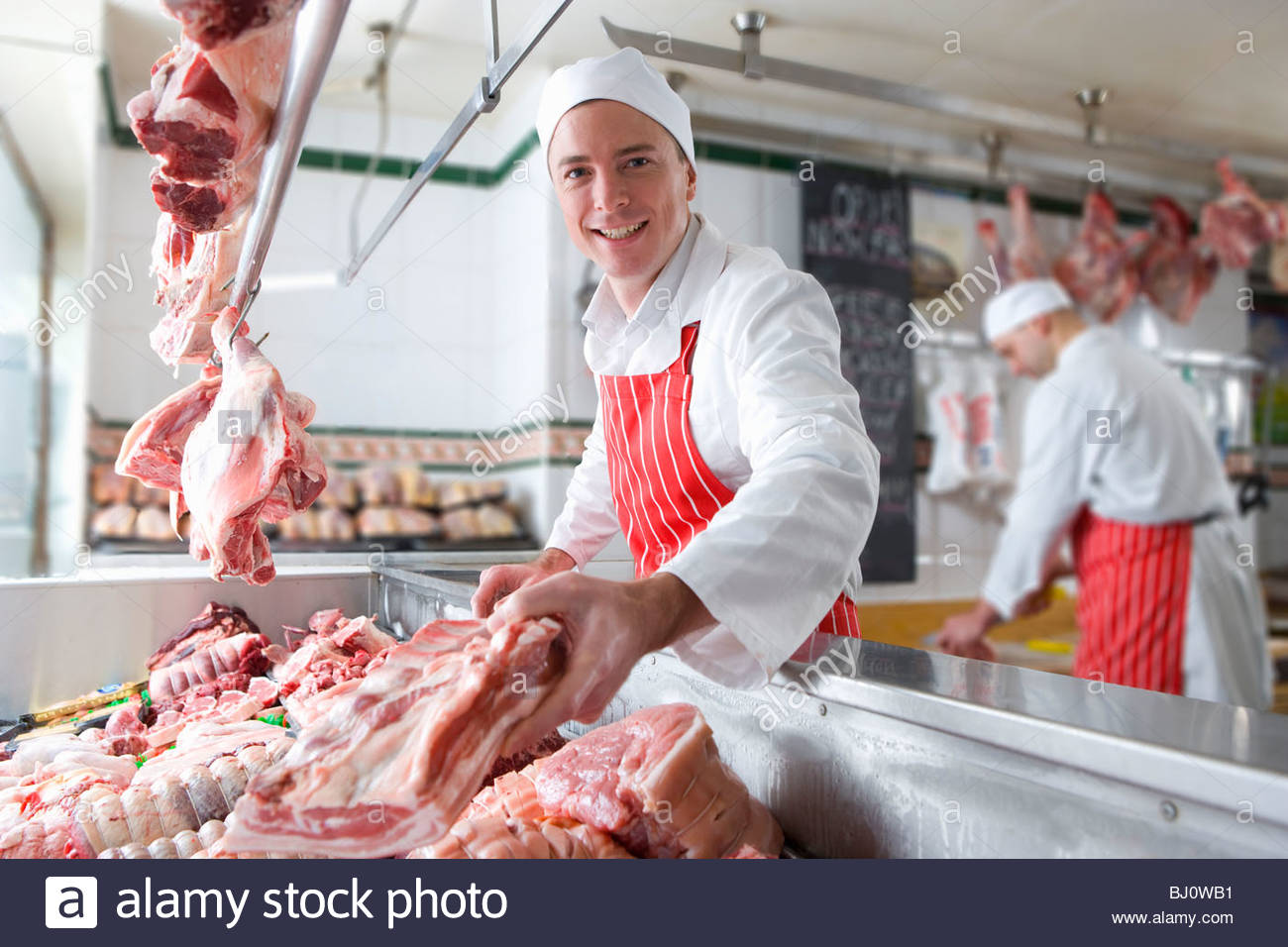 Smiling butcher arranging meat in display case Stock Photo, Royalty ...