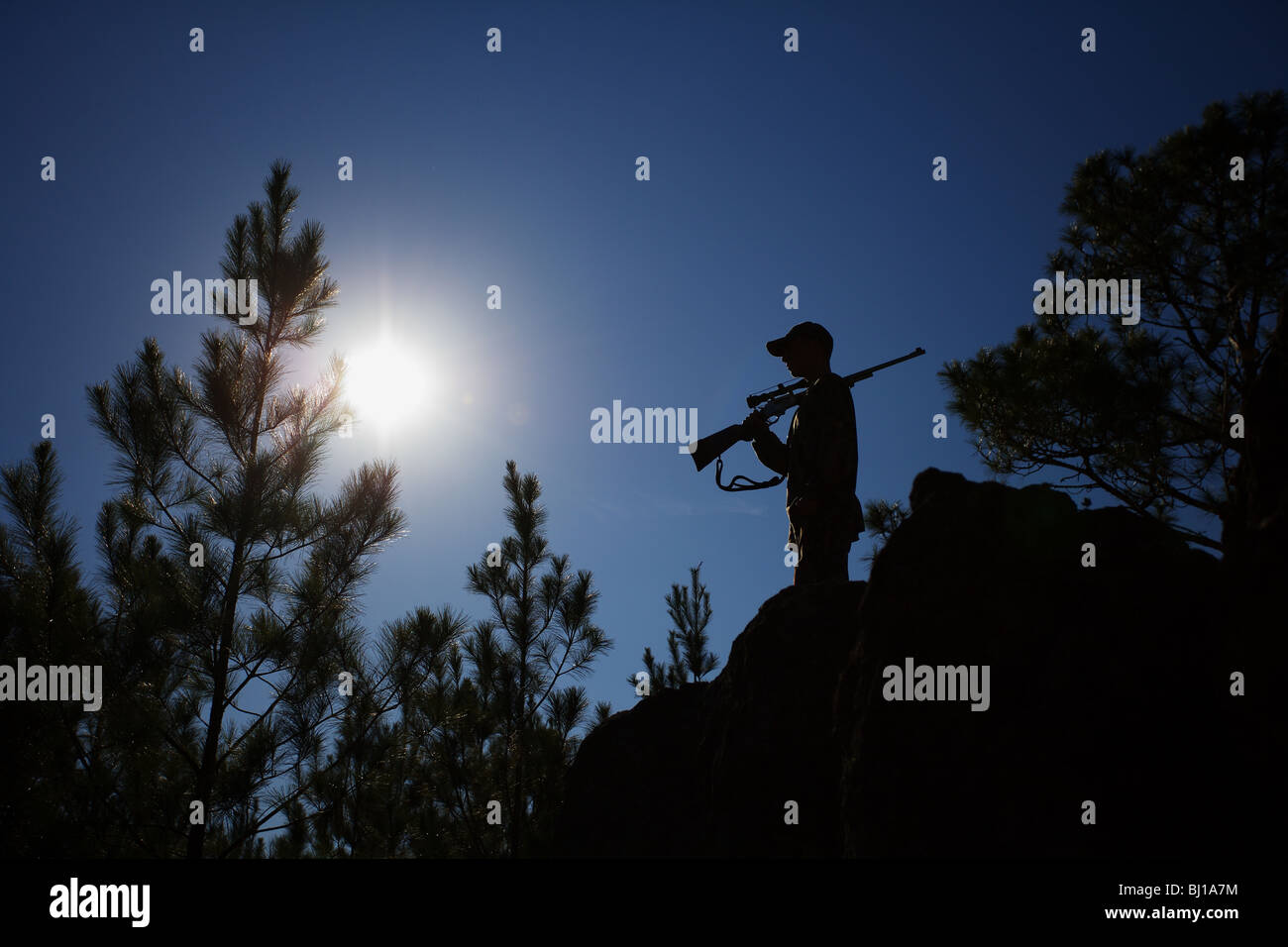 SILHOUETTE VIEW HUNTER STANDING ON ROCKY CLIFF HOLDING WEAPON ON ...