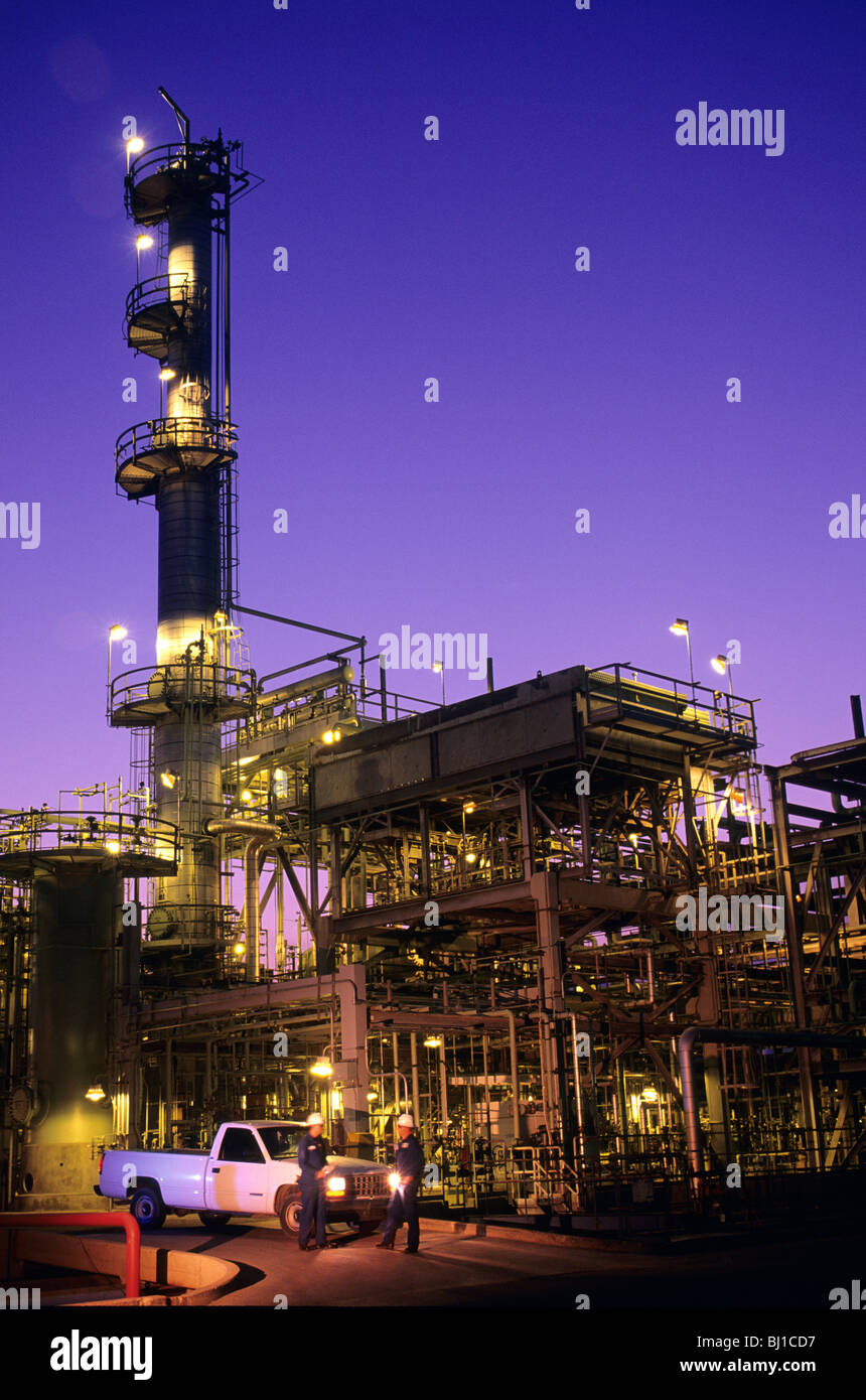 two refinery workers standing by a pickup truck with oil refinery ...