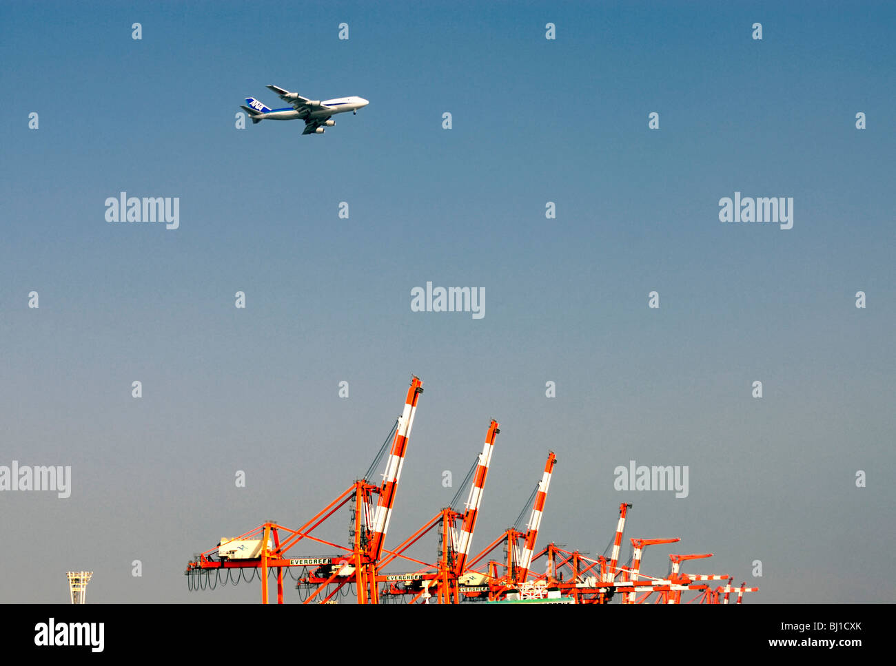 A plane flies over cranes used for loading cargo onto ships in Tokyo ...