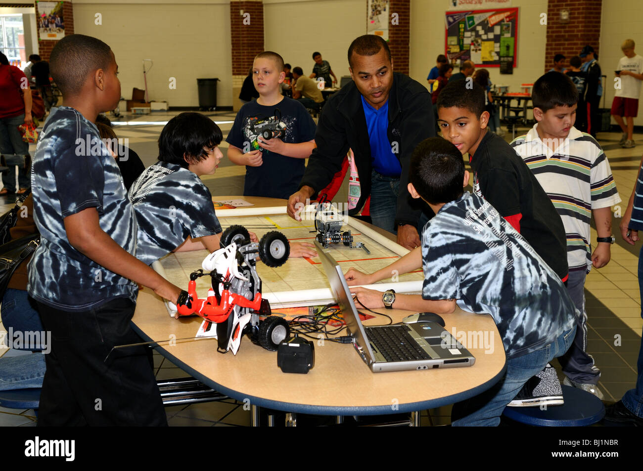 Parent coaches a group of school kids building and testing Lego robot ...