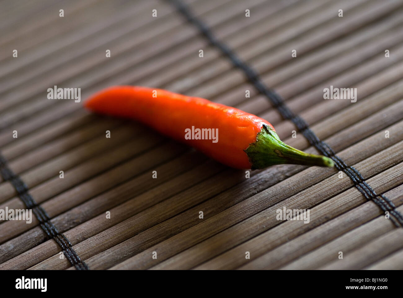 A single red chilli on a bamboo surface Stock Photo - Alamy