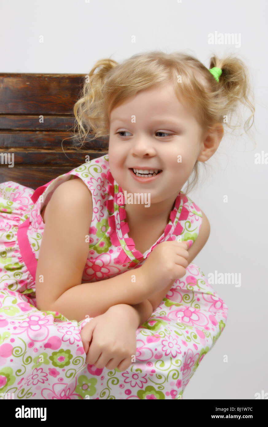 A three year old blond little girl, smiling as she leans on the seat of ...