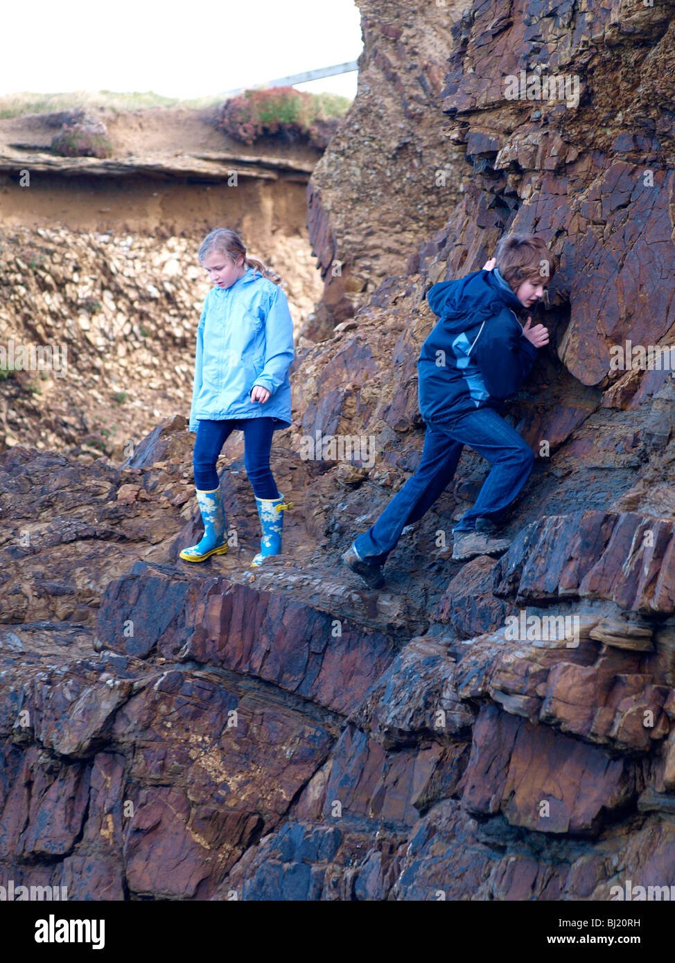 Two children climbing along cliff ledge, Cornwall, UK Stock Photo - Alamy