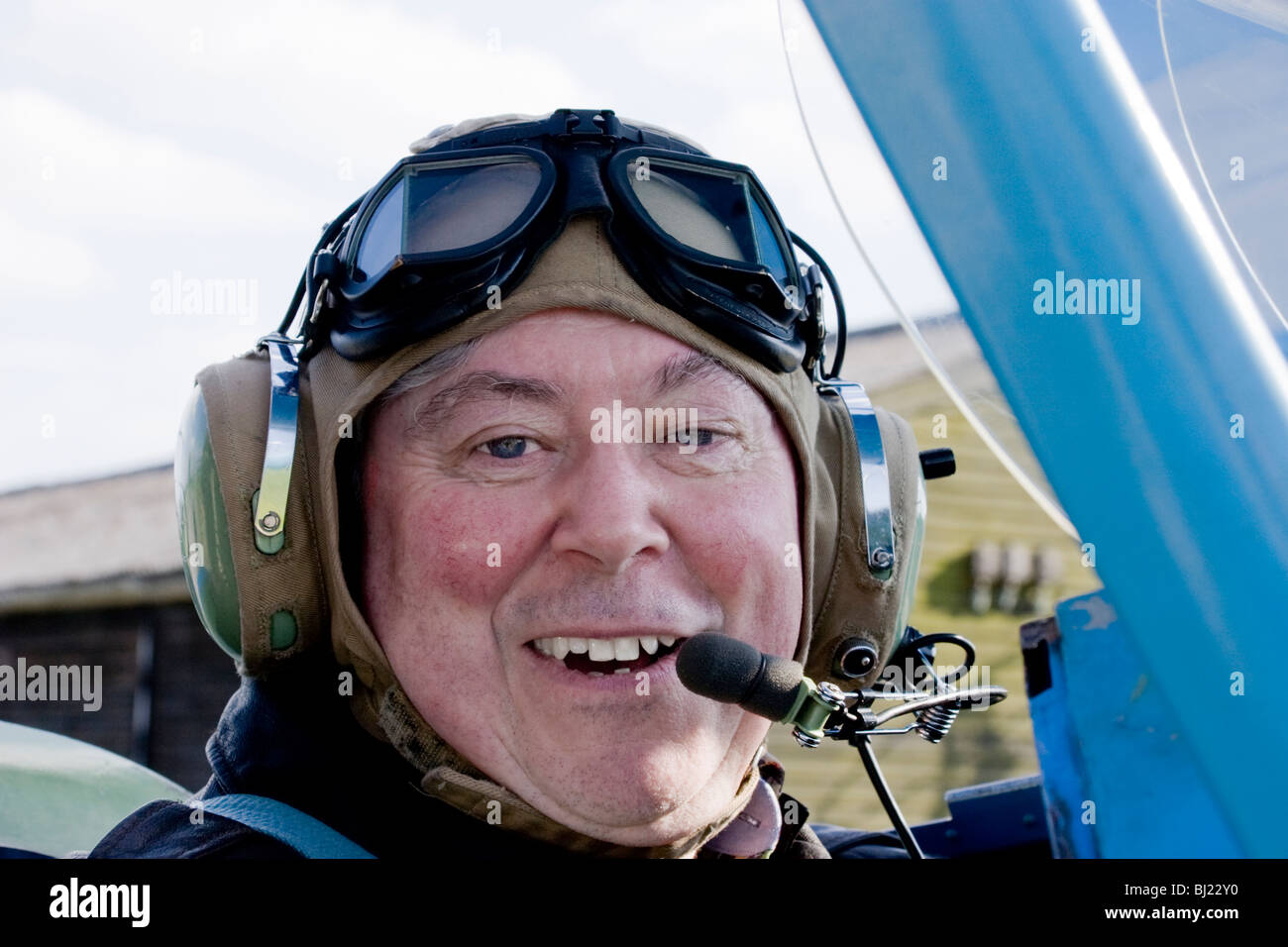Mature pilot with flying helmet at the controls of an open cockpit ...