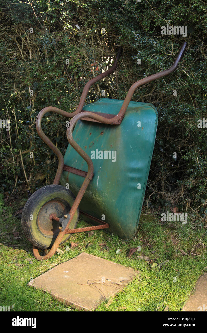 Wheelbarrow tipped up against a garden hedge Stock Photo - Alamy