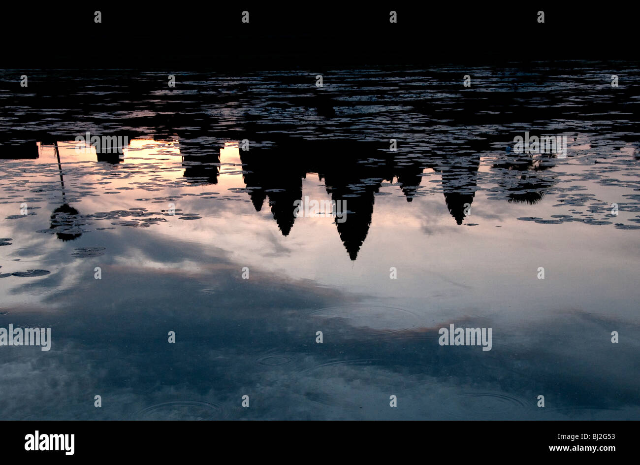 The reflection of a silhouetted Angkor Wat in the water at sunrise ...
