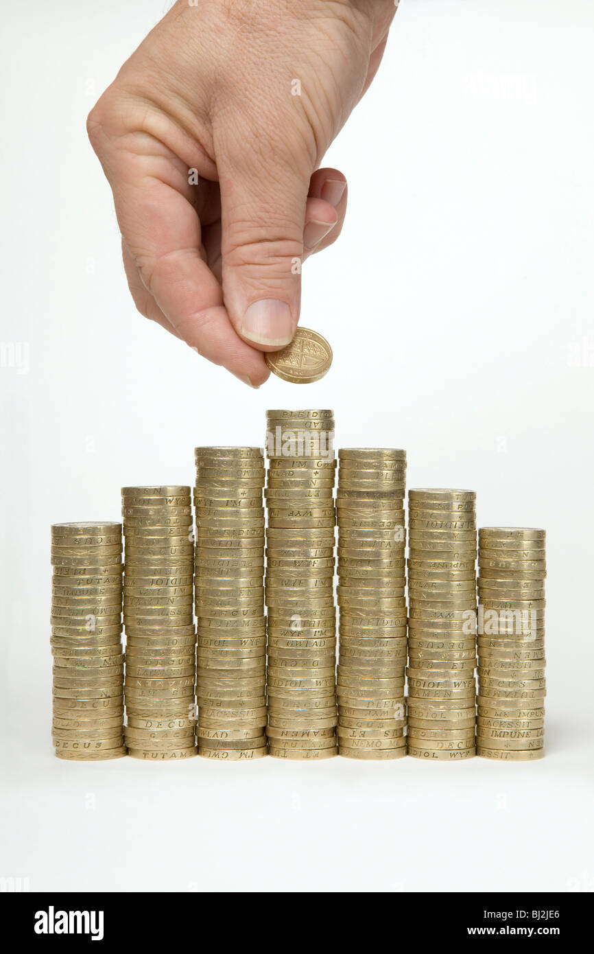 Seven stacks of pound coins with hand placing coin on centre stack on ...
