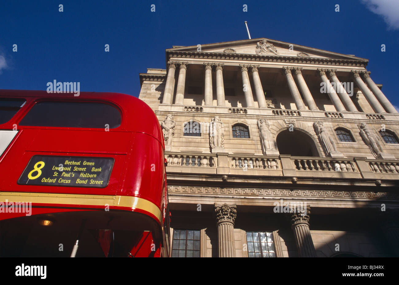A number 8 red London bus passes the pillars of the famous Bank of ...