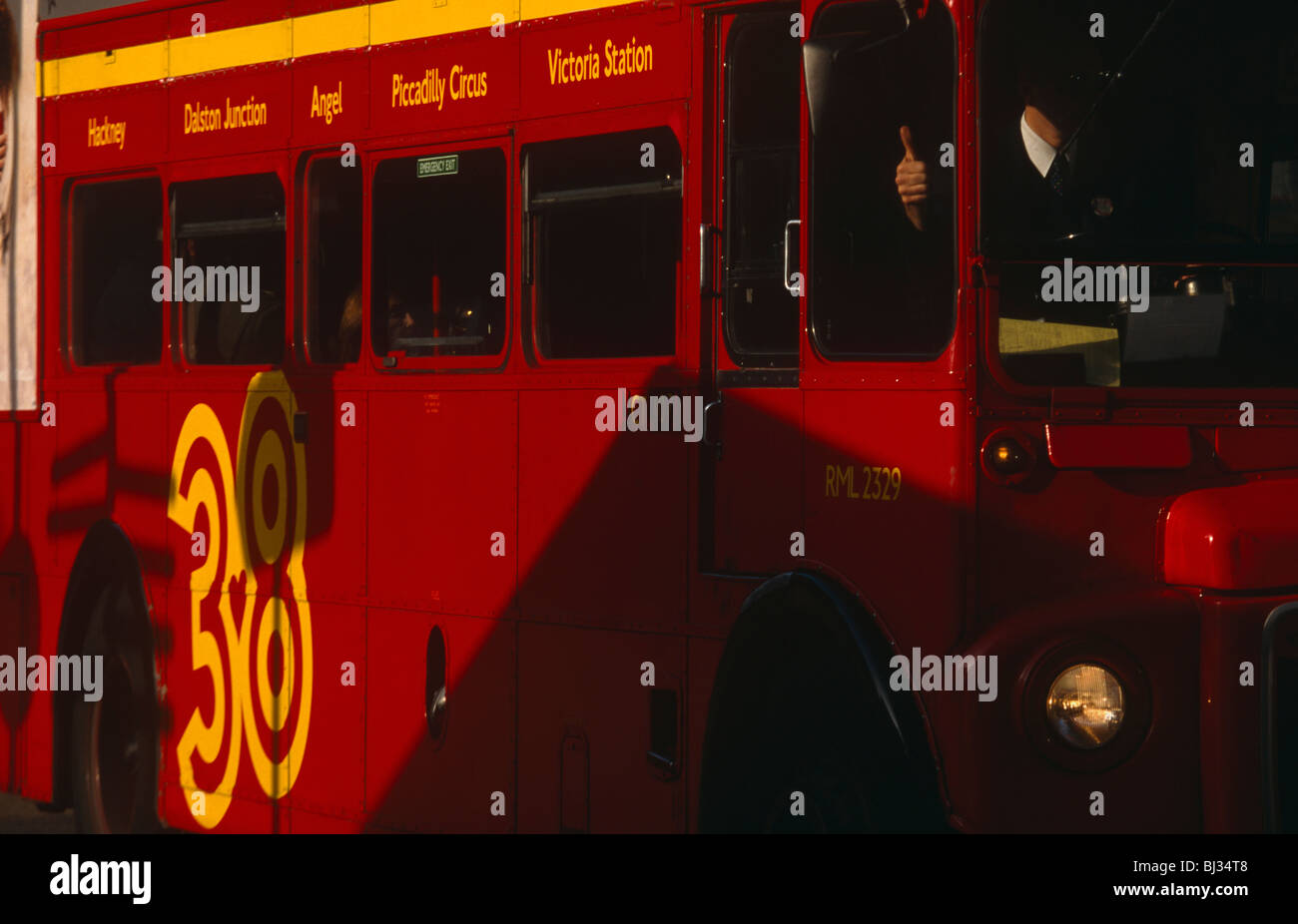 Driver of a number 38 red London bus which is passing between sunlight ...