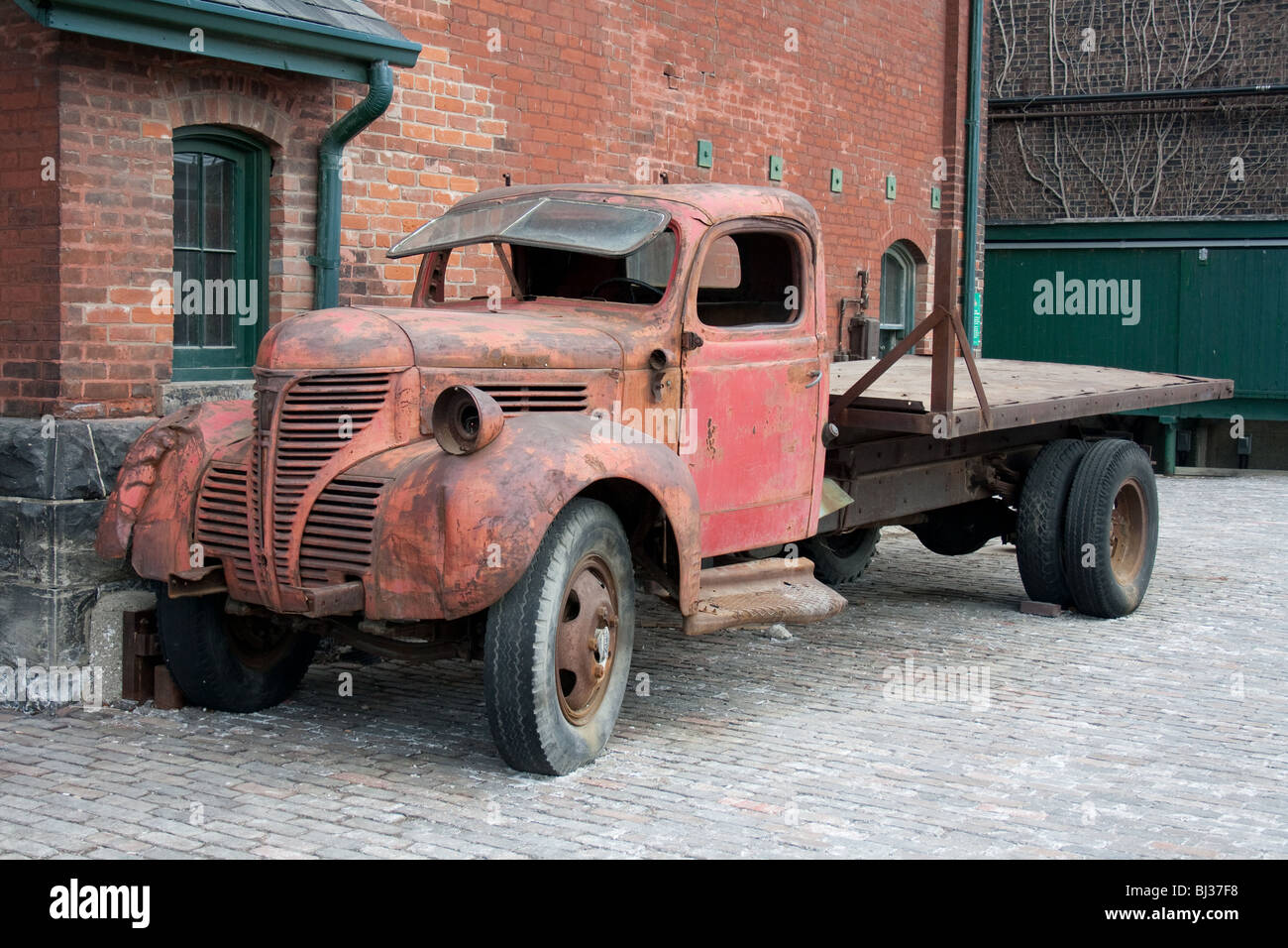 A red old rusted truck parked outside of an old red brick factory at ...