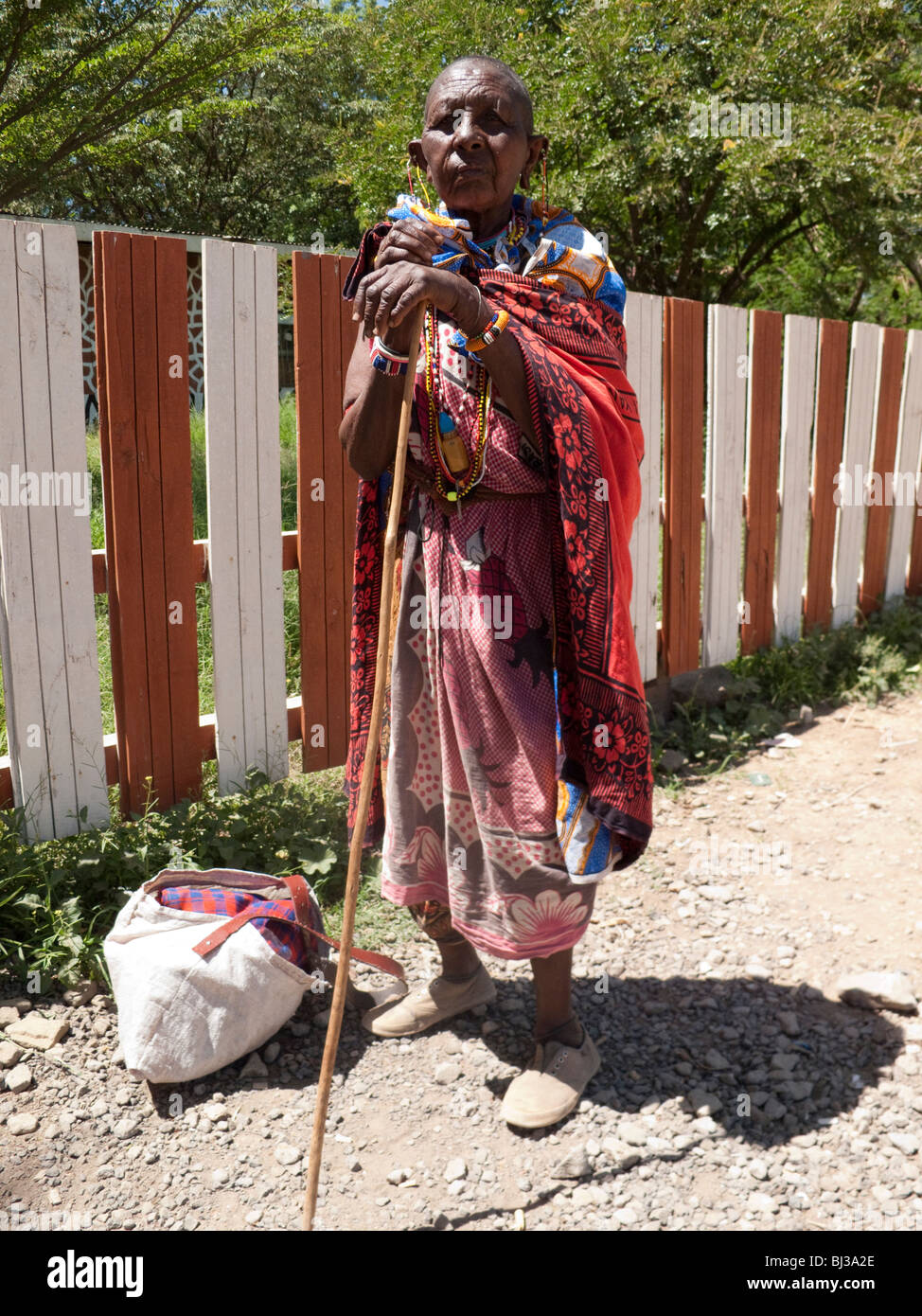 Old bald Masai woman leaning on a staff by a fence Kenya East Africa ...