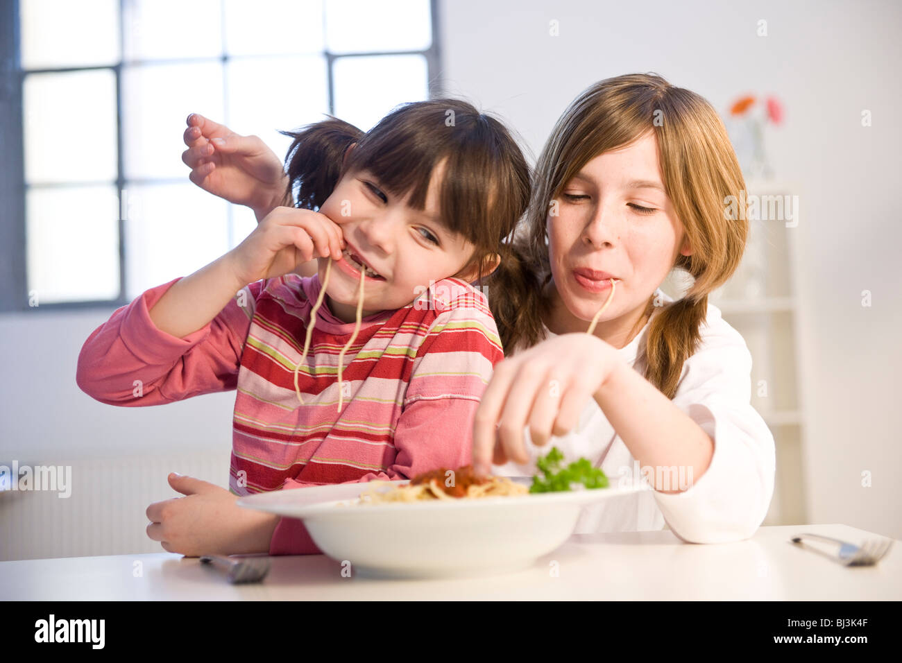 Two girls eating spaghetti together Stock Photo - Alamy