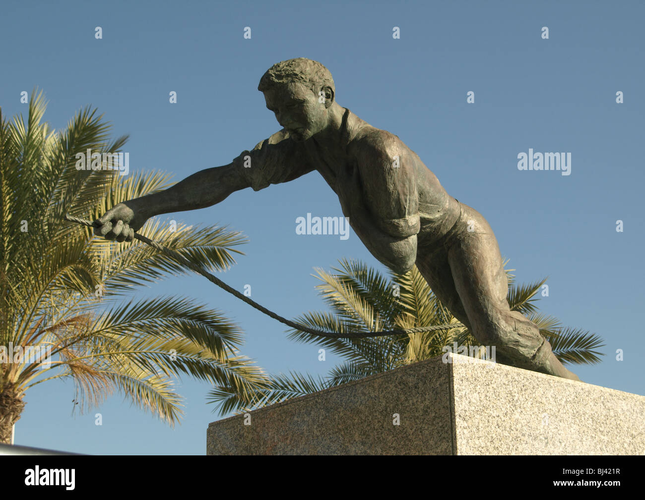 Statue of Spanish fisherman on tall stone plinth leaning forward as if ...