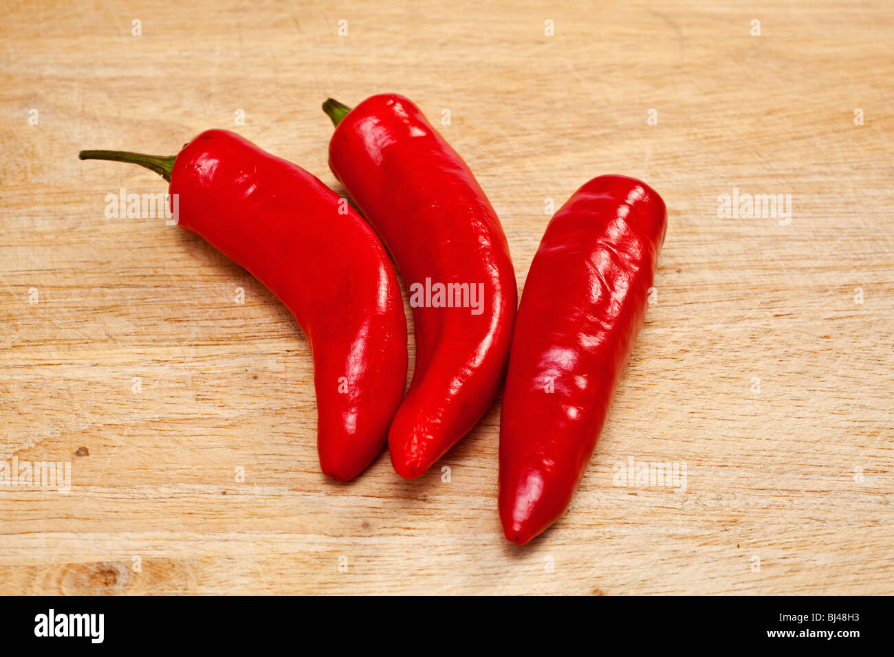 three red chilli peppers on a chopping board Stock Photo - Alamy