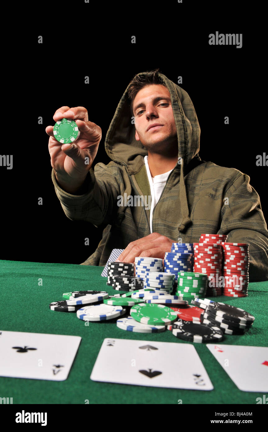Young man playing poker and holding some chips against a black ...