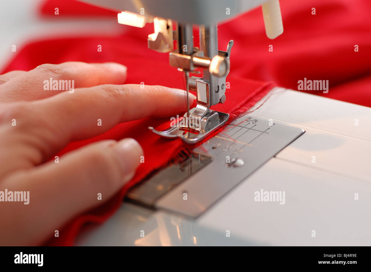 A hand of a dressmaker supporting a cloth while sewing on a sewing ...