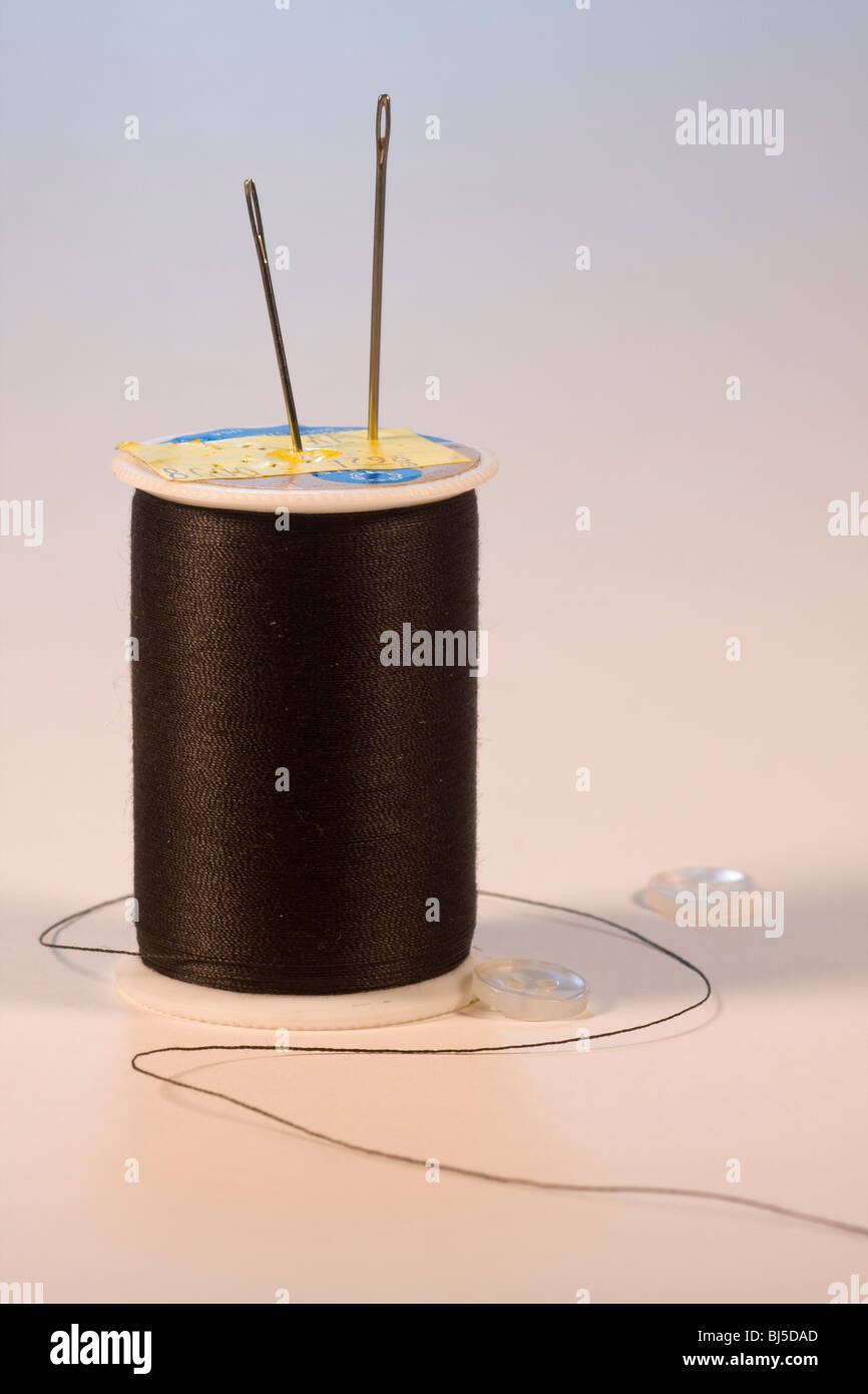 Spool of black sewing thread with needles and two buttons on white ...