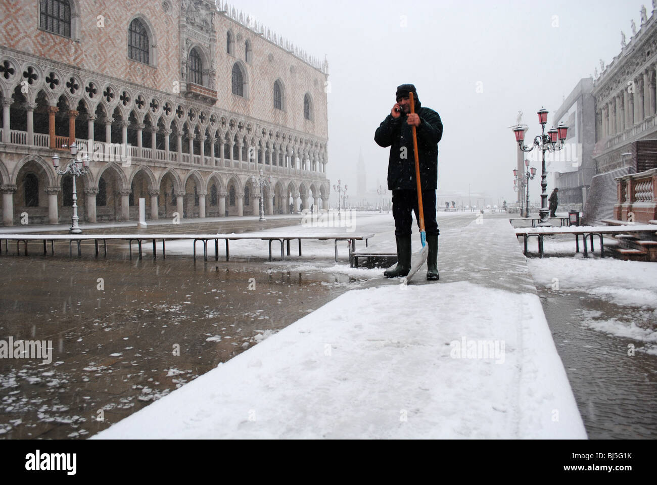 A man clears snow from walkways in a flooded St Mark's Square, Venice ...