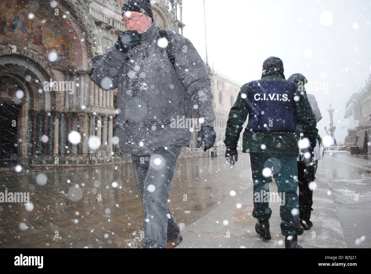 Men walk along a walkway during a snow storm in a flooded St Mark's ...