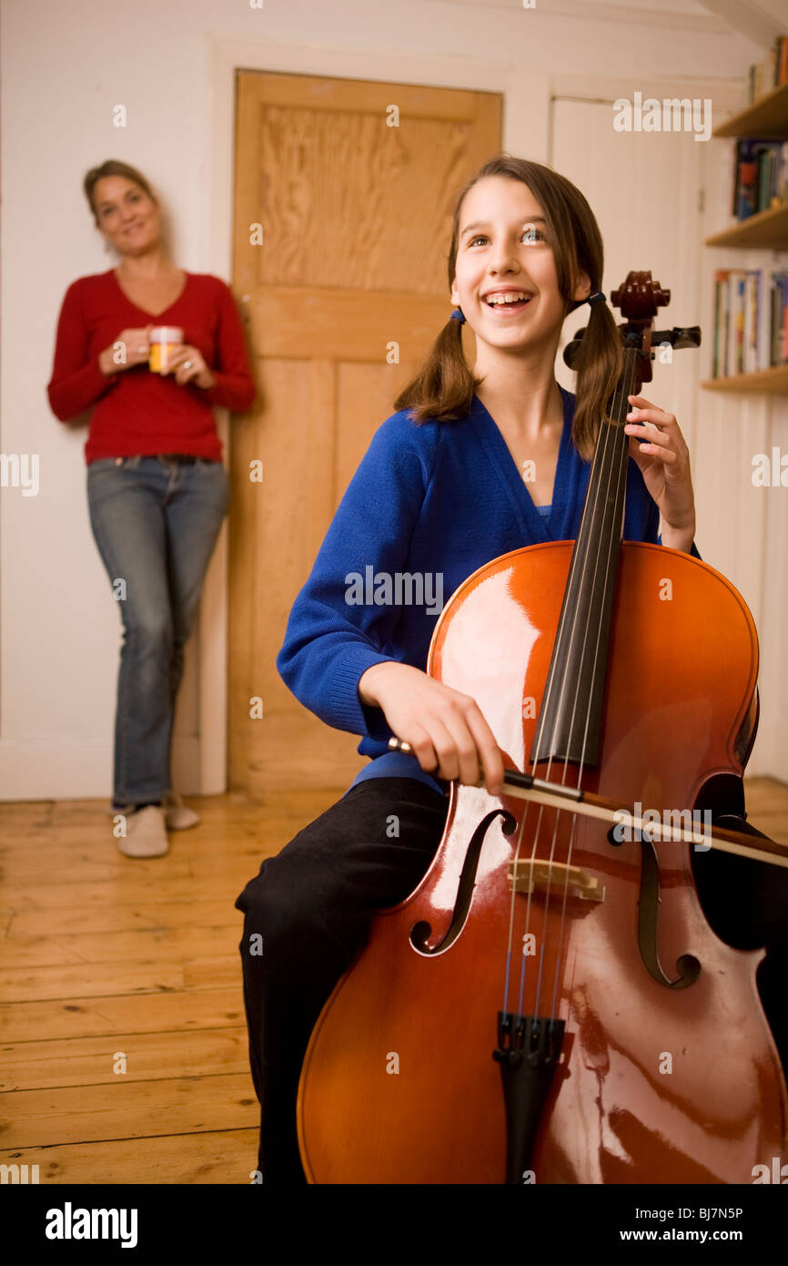 Girl practicing playing the cello at home with her mother Stock Photo ...