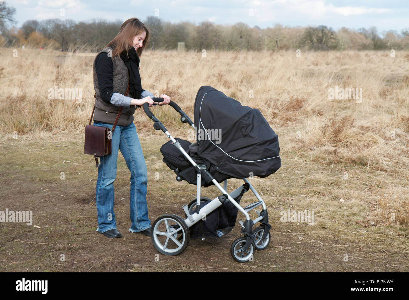 Happy young Mother walking and pushing a pushchair in Richmond Park ...