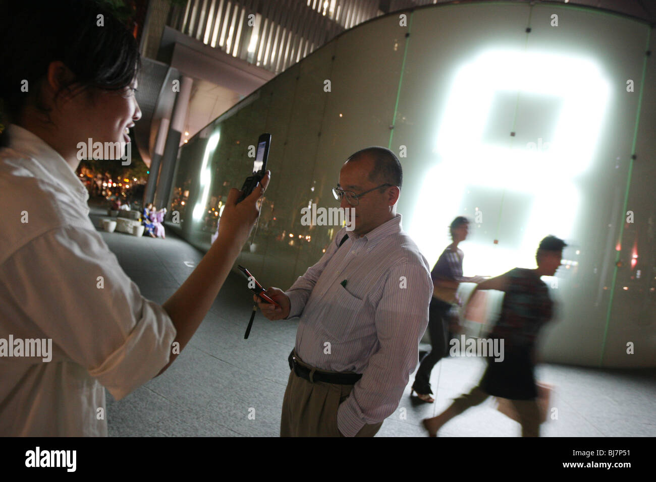 Japanese people using mobile telephone in front of digital number ...