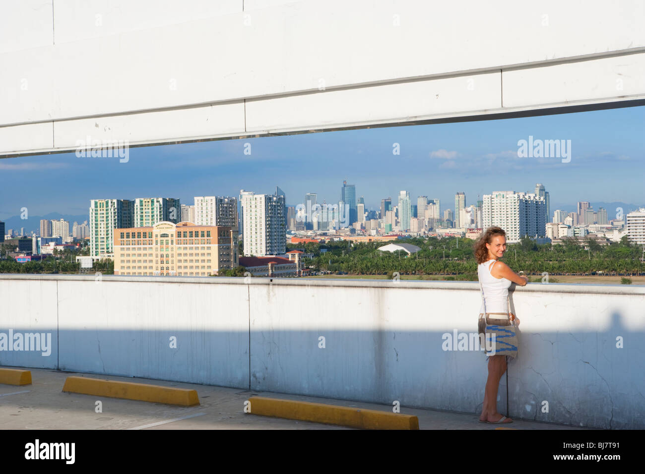 Girl smiling and looking round Manila skyline through panoramic window ...
