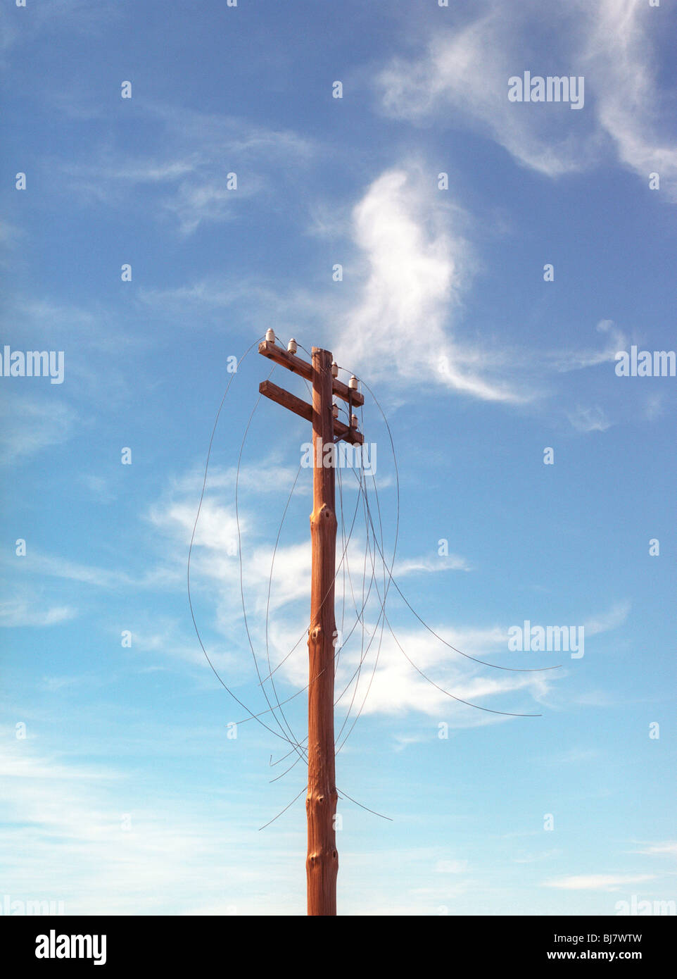 Disused telephone pole seen against the sky with cut wires hanging down ...