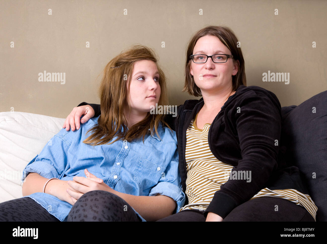 Mother and daughter sitting in sofa. Mother has an absent look Stock ...