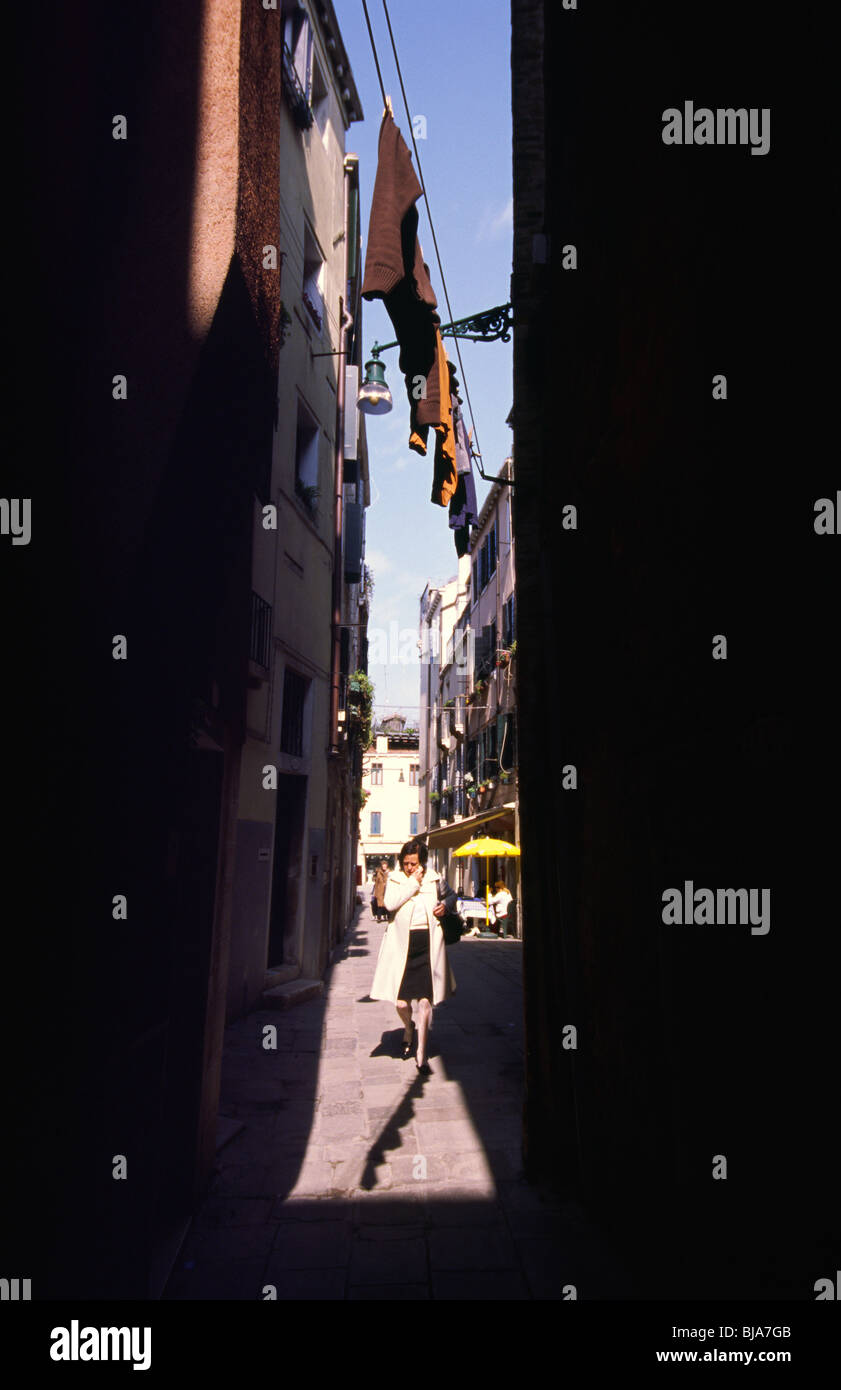 Venetian street scene. Woman walks under washing lines through narrow ...