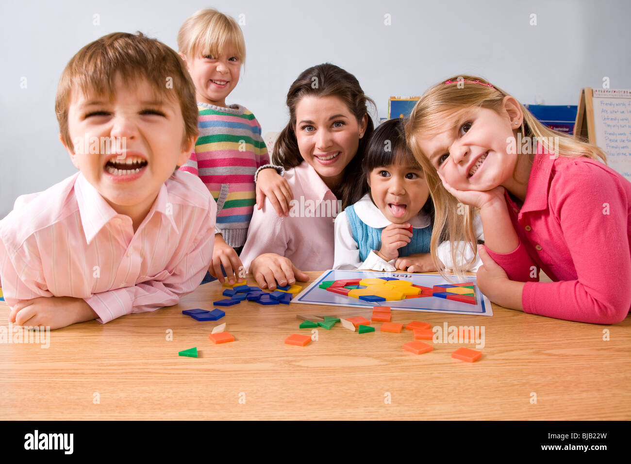 Smiling teacher helping cute preschool children with colorful shapes ...