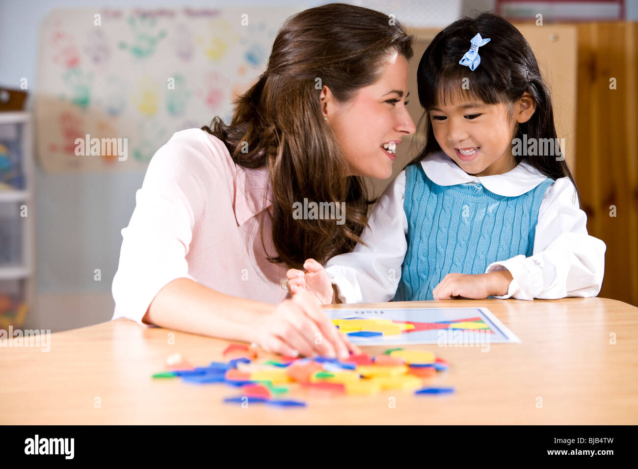 Preschool teacher helping little Asian girl with colorful shape puzzle ...