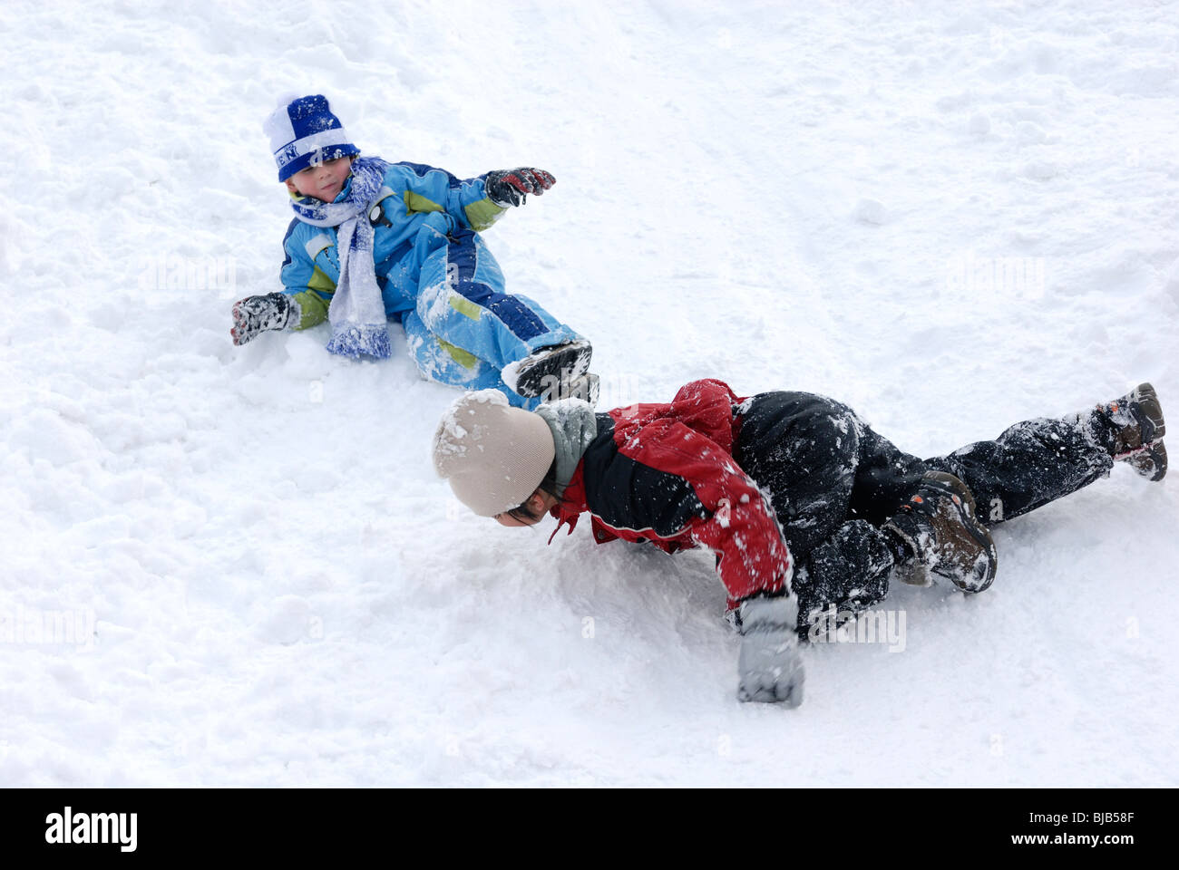 Laughing child boy sliding down a snow covered hill and playing in snow ...