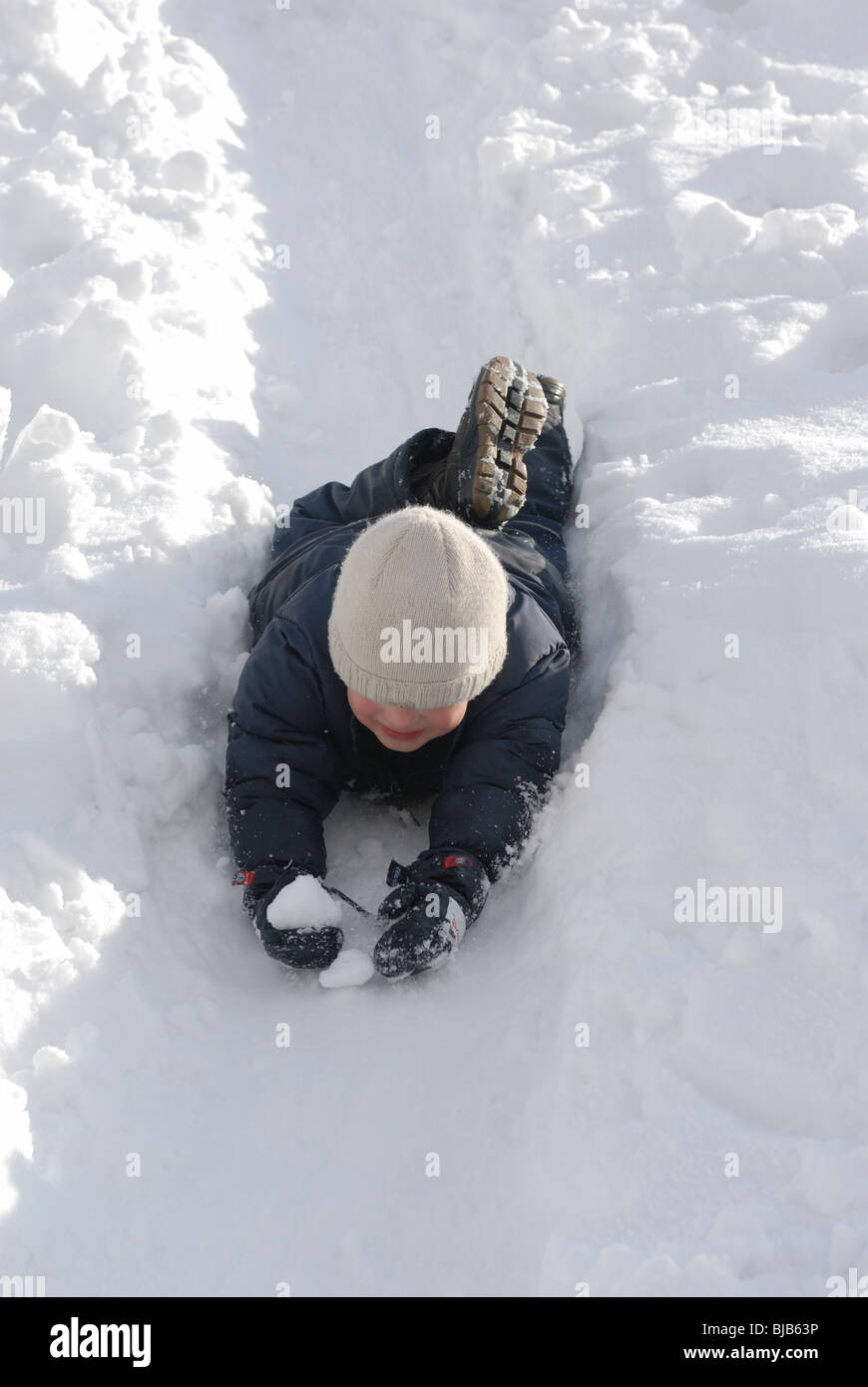 Laughing child boy sliding down a snow covered hill and playing in snow ...