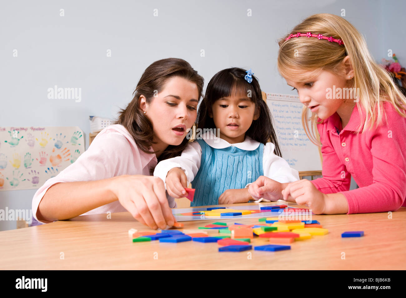 Smiling teacher helping cute little preschool girls with colorful ...