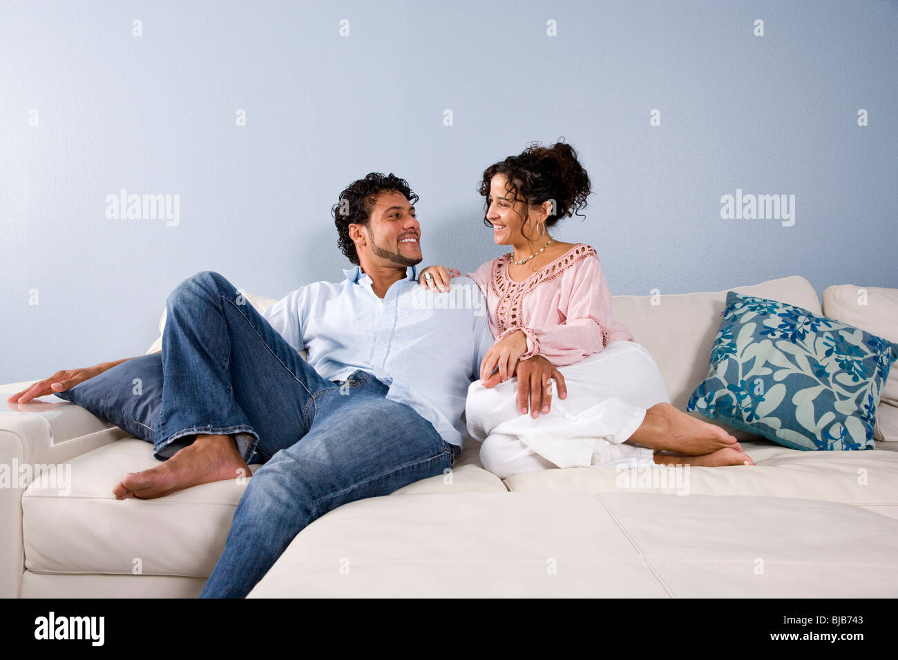 Young Hispanic couple sitting together on white couch Stock Photo - Alamy