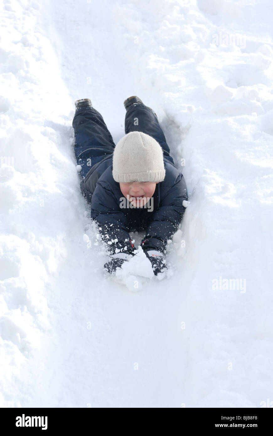 Laughing child boy sliding down a snow covered hill and playing in snow ...