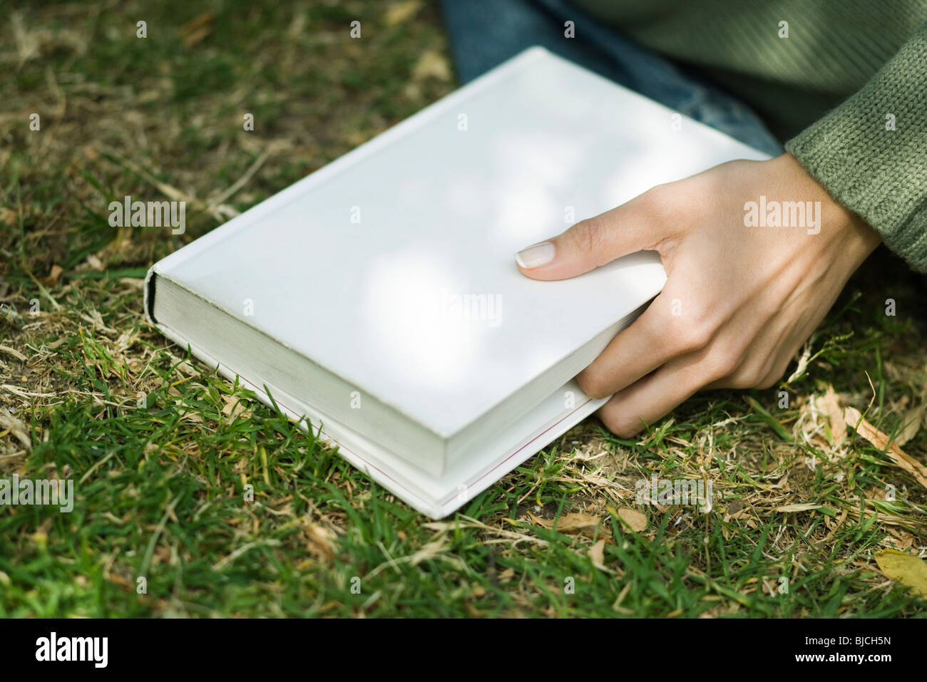 Woman holding closed book, marking place with finger Stock Photo - Alamy