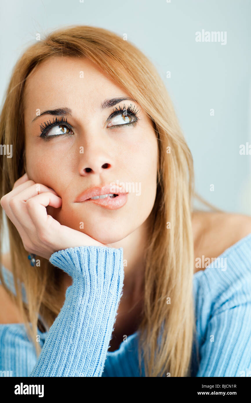 portrait of woman thinking and biting her lips, looking up with hand on ...