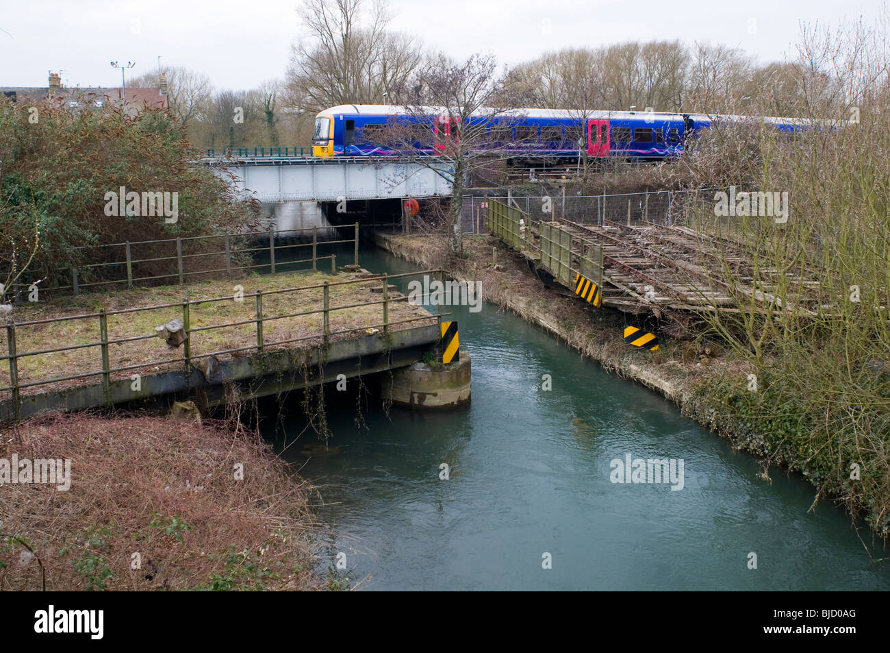 A local train passing a disused and derelict rail swing bridge over the ...