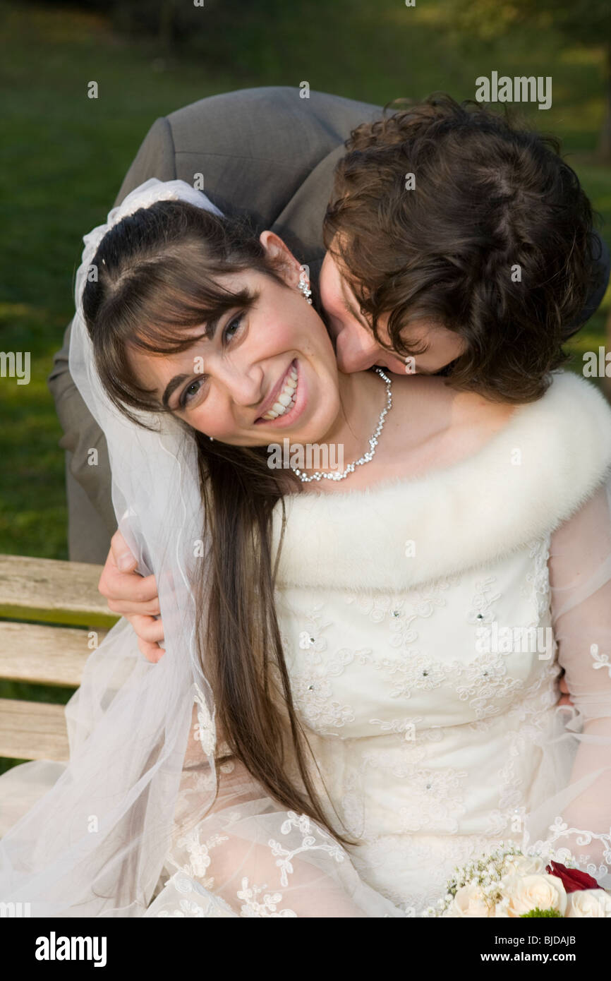 Bridegroom kissing his bride on the neck while she is looking at camera ...