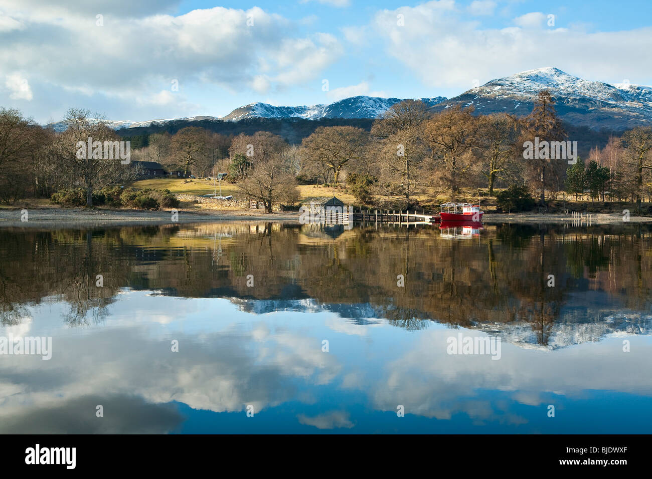 Reflection of sky, trees and mountains on Coniston Water in winter with ...