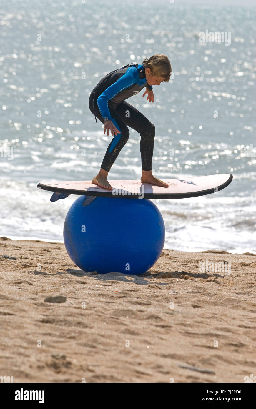Young boy on beach balancing his surfboard on top of rubber ball during ...
