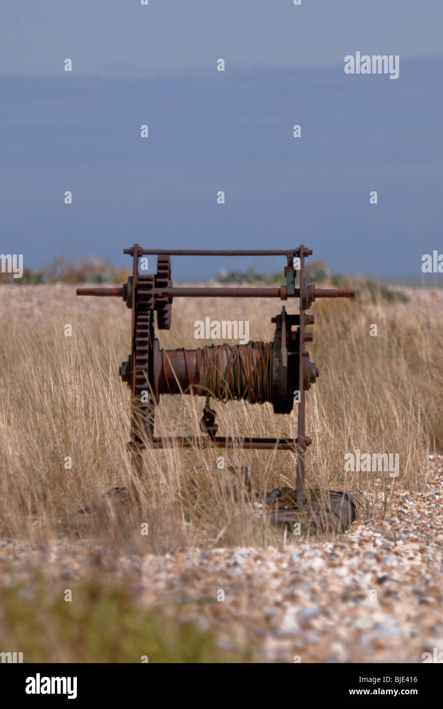 Boat winch rusting against a blur sky, on pebble beach with grass Stock ...